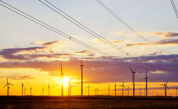 Stromleitung und Windkraftanlagen mit untergehender Sonne im Hintergrund